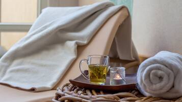 Ambiente de spa com cadeira de massagem, bandeja com chá, toalha enrolada e vela.