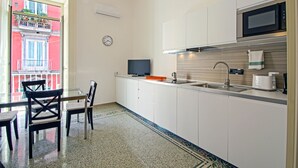Cozinha moderna com armários brancos, micro-ondas e pia. Há uma mesa de jantar com cadeiras e um relógio na parede.