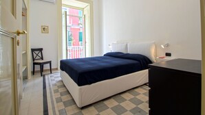 Quarto com cama, cadeira, cômoda e janela com vista para um edifício.