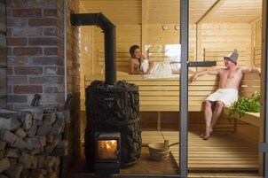 Uma sala de sauna com estufa a lenha, bancos e parede de tijolos.