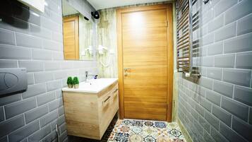 Um banheiro com porta de madeira, pia com espelho e chão revestido de azulejos.