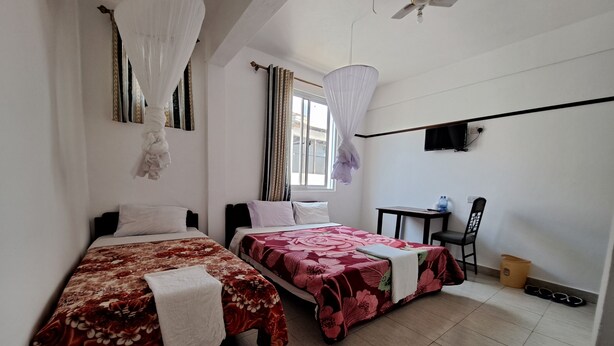 Quarto com duas camas, ventilador de teto, televisão e uma mesinha.