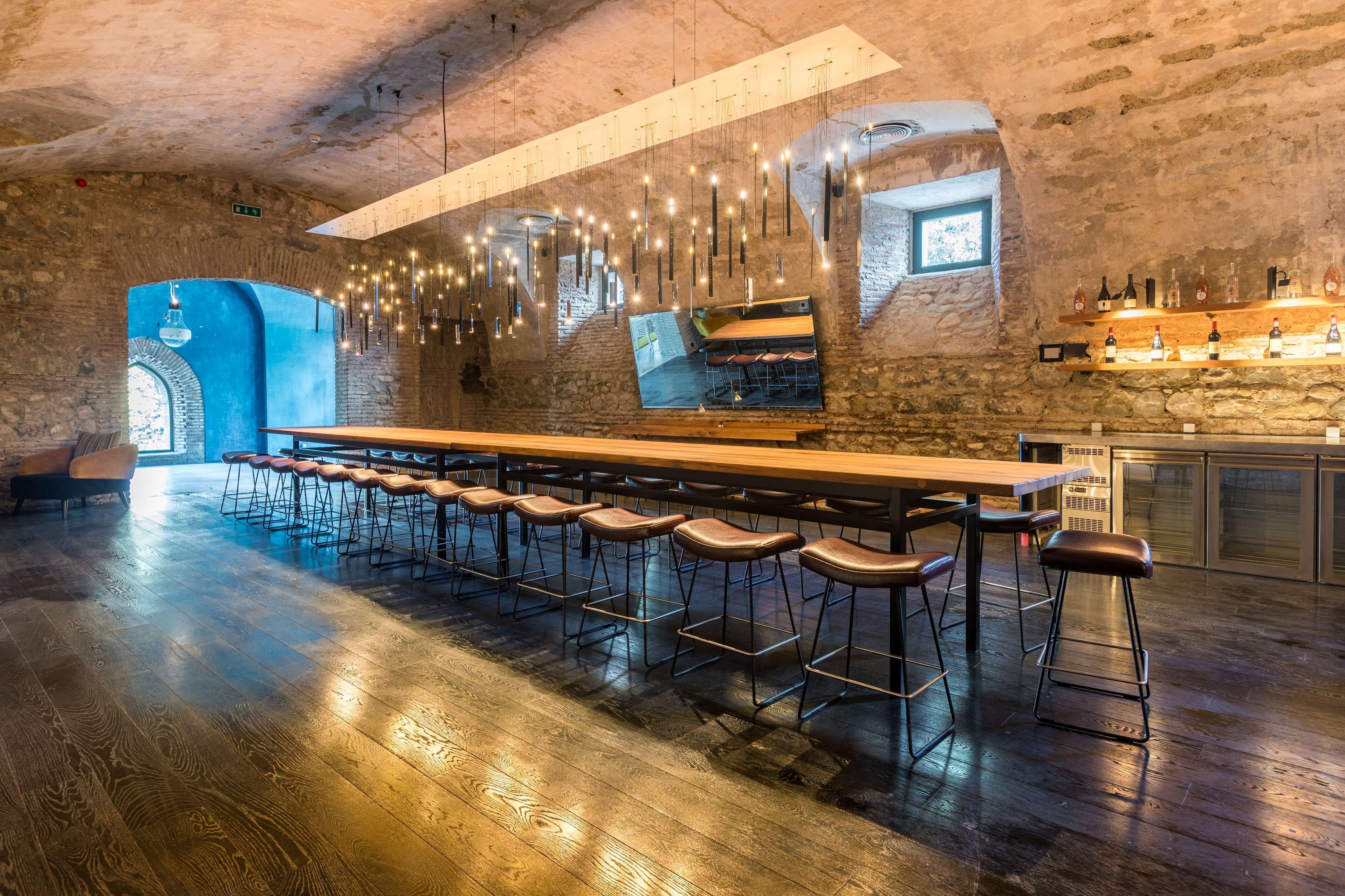 Uma área de bar com um balcão comprido, vários bancos e um painel de parede de pedra.