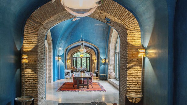 Interior com área de jantar, paredes de pedra e um teto abobadado grande.