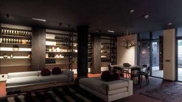 Um interior moderno com sofá, um banquinho, mesa de jantar, cadeiras e uma coleção de vinhos nas prateleiras.