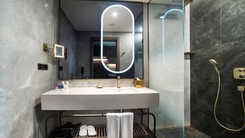 Casa de banho moderna com um espelho grande, uma luz redonda acima do espelho, um chuveiro manual e um porta-toalhas com toalhas.