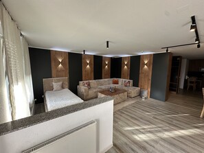 Quarto moderno com cama, sofá e mesa de centro, painéis de parede de madeira e luminárias de teto.