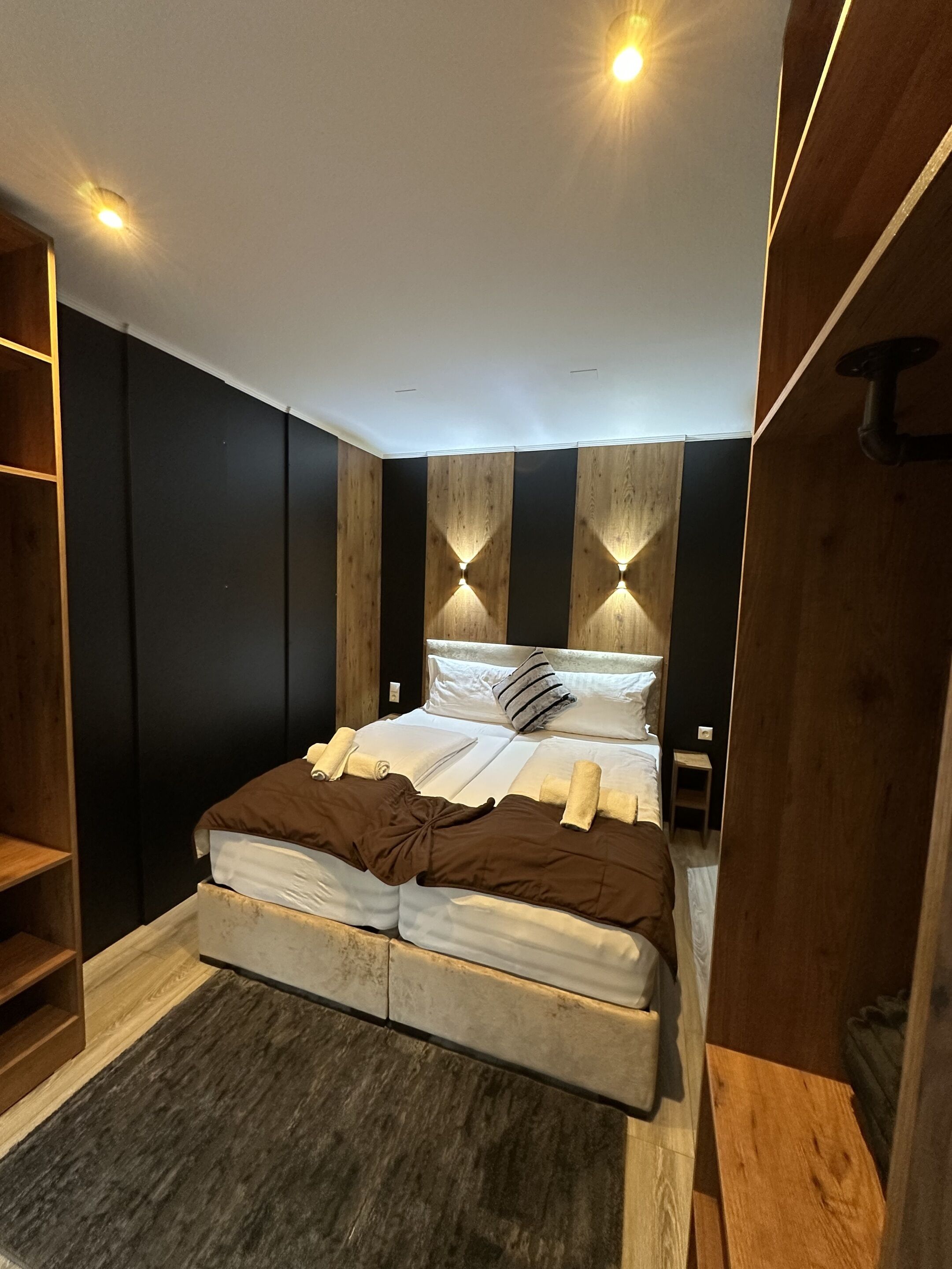 Quarto moderno com cama, painéis de madeira e iluminação embutida.