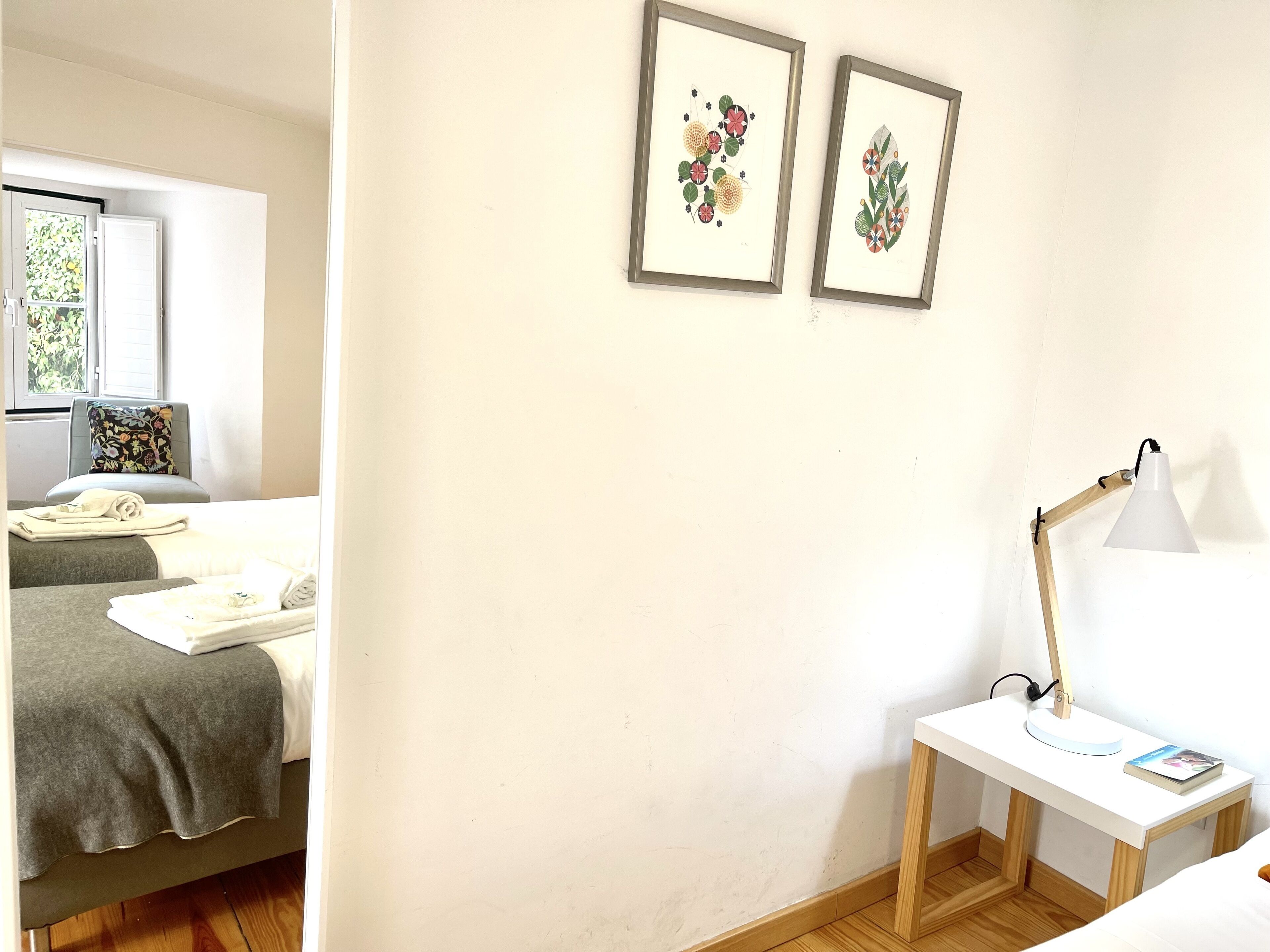 Quarto com cama, mesa de cabeceira com abajur e duas gravuras botânicas emolduradas na parede.
