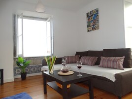 Uma sala de estar com sofá, mesa de centro, planta em vaso e um quadro na parede.