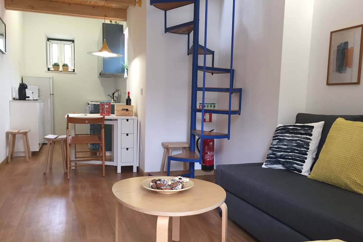 Um espaço de estar compacto com cozinha, mesa de jantar, sofá e escada espiral azul.