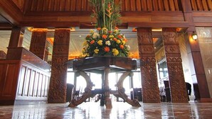 Um lobby com teto de madeira, arranjo floral central e piso polido.
