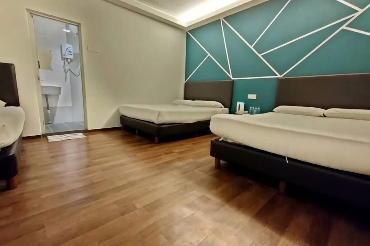 Quarto de hotel com duas camas, piso de madeira, banheiro com chuveiro e uma parede em tom de verde-água.