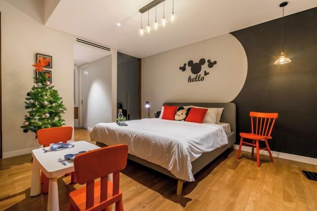 Quarto moderno com cama, mesa de jantar e cadeiras. Há uma árvore de Natal e uma parede com um letreiro que diz 'hello'.
