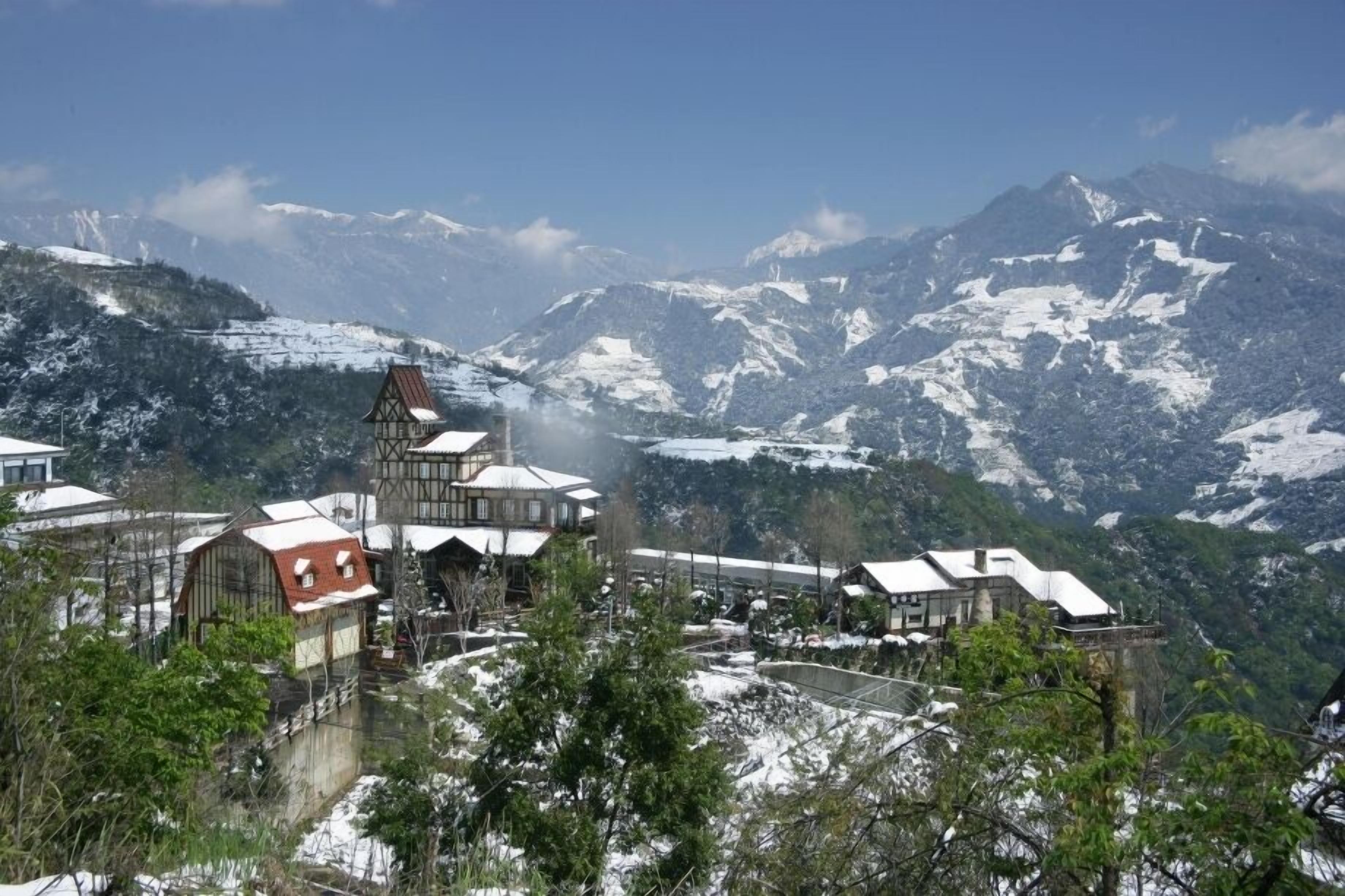 Uma pousada de montanha com arquitetura tradicional, rodeada por picos nevados e um céu claro.