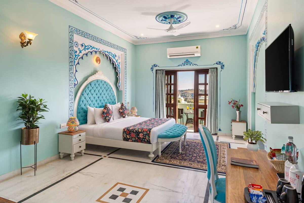 Quarto com cama, mesas de cabeceira, escrivaninha, cadeira, televisão e janela com vista.