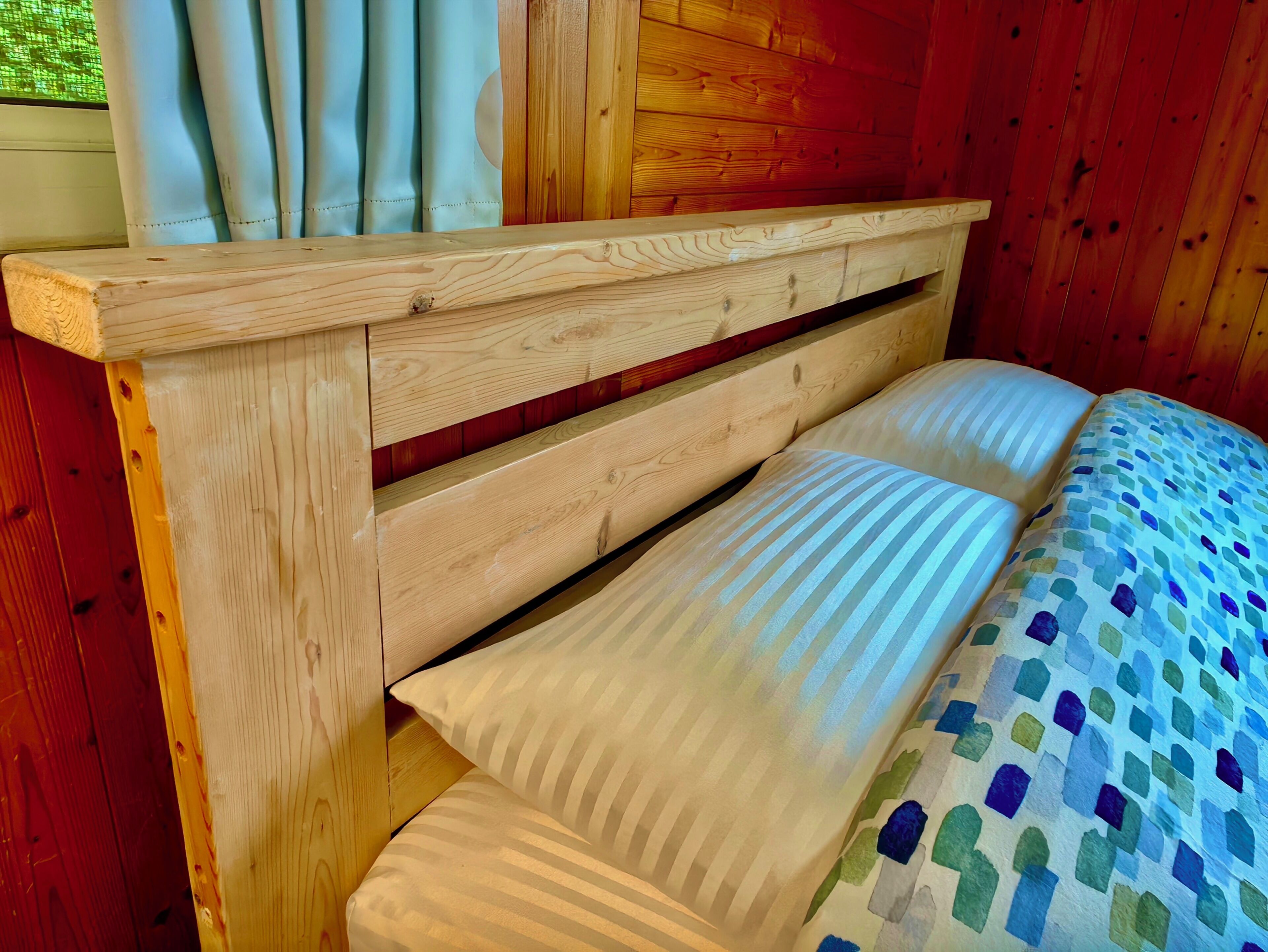 Uma cama de madeira com cabeceira, uma janela com cortinas e um edredom estampado.