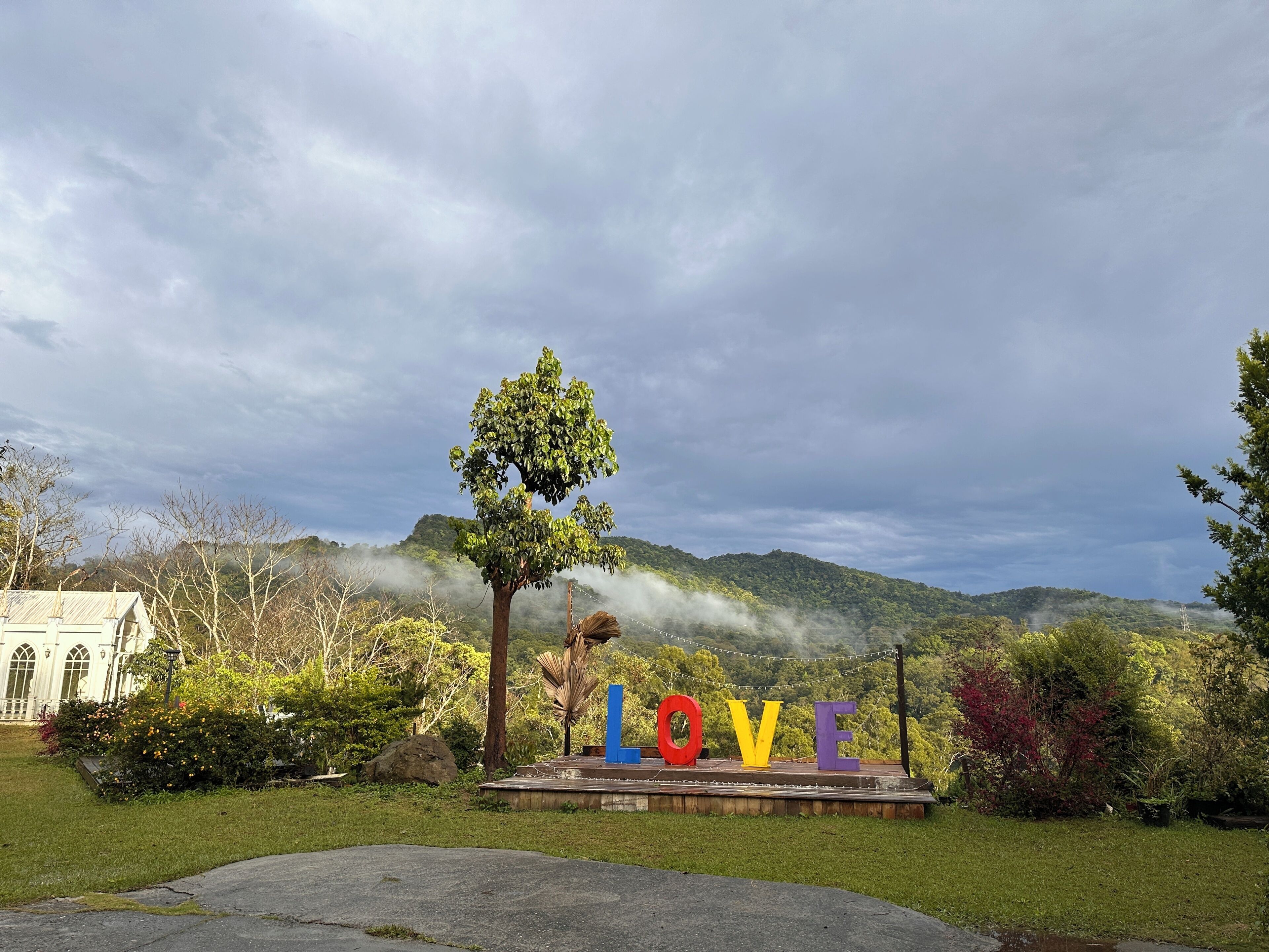 Um jardim com um letreiro 'LOVE', uma árvore e um edifício ao fundo.