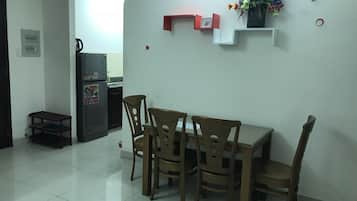 Uma área de refeições com uma mesa e quatro cadeiras, um refrigerador, uma pequena prateleira com um relógio e uma planta em vaso na parede.