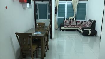 Uma sala de jantar com mesa, cadeiras, um sofá e uma janela com cortinas.