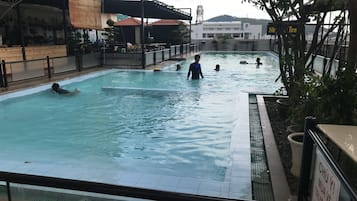Uma piscina ao ar livre com bordas azulejadas, rodeada por um guarda-corpo de metal.