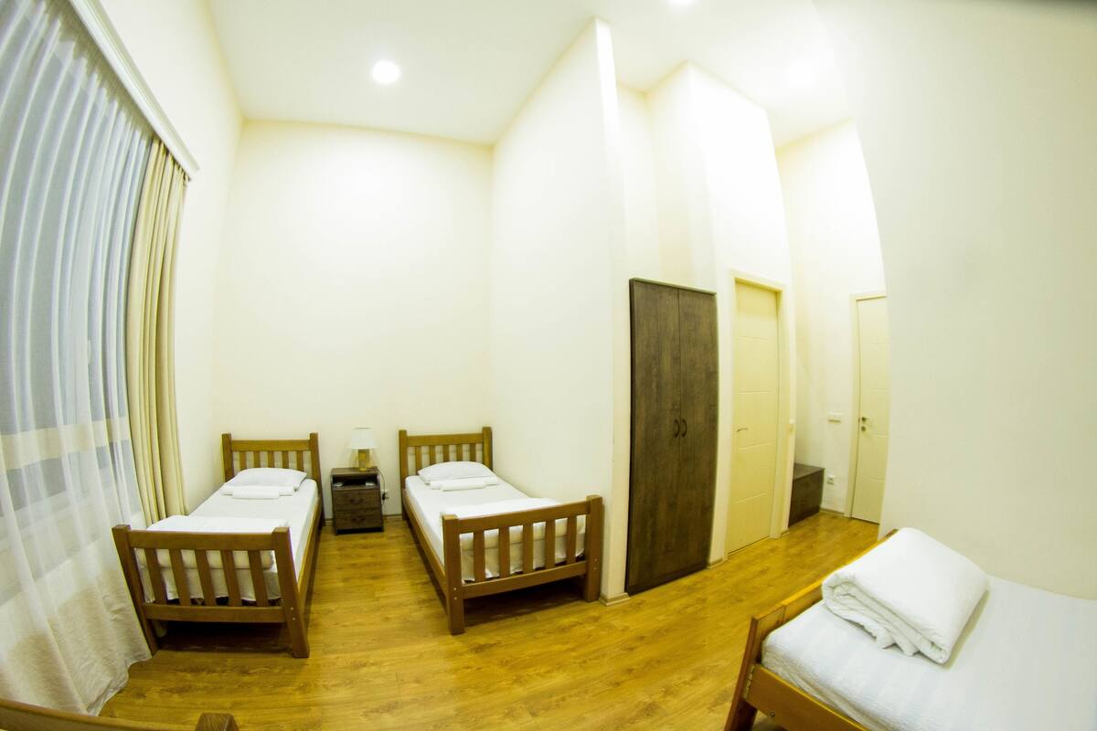 Um quarto pequeno e claro, com duas camas de madeira, um banco de madeira e uma cadeira.