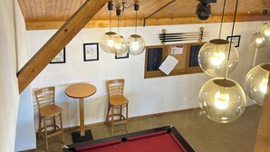 Teto de madeira com mesa de bilhar, duas cadeiras e luminárias pendentes esféricas.