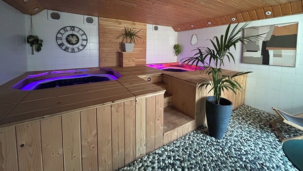 Uma área de spa com madeira, duas banheiras de hidromassagem, um relógio e um vaso de planta.