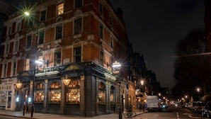 Um edifício histórico com fachada clássica, iluminado por postes de rua, com uma entrada imponente e uma placa com a inscrição "The Old School".