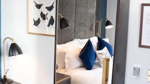 Quarto com cama, abajures, um quadro com pássaros e luminária na parede.