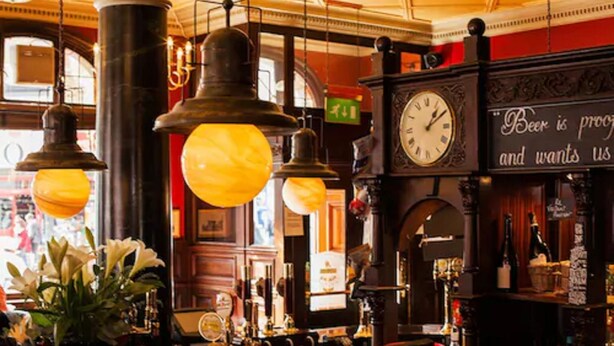 Um bar com lustres de latão pendurados, um relógio e uma placa que diz 'A cerveja é a prova e quer nos ter'.