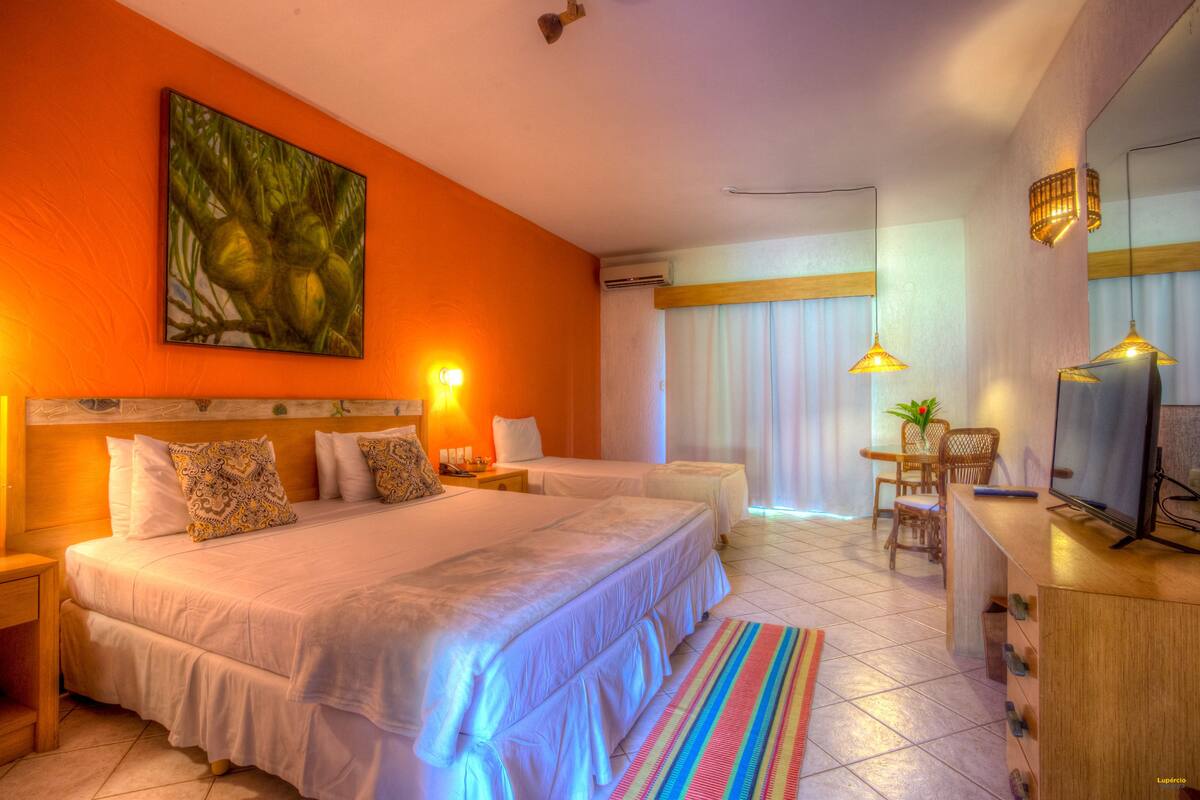 Quarto de hotel com uma cama grande, uma escrivaninha com televisão e um quadro na parede.