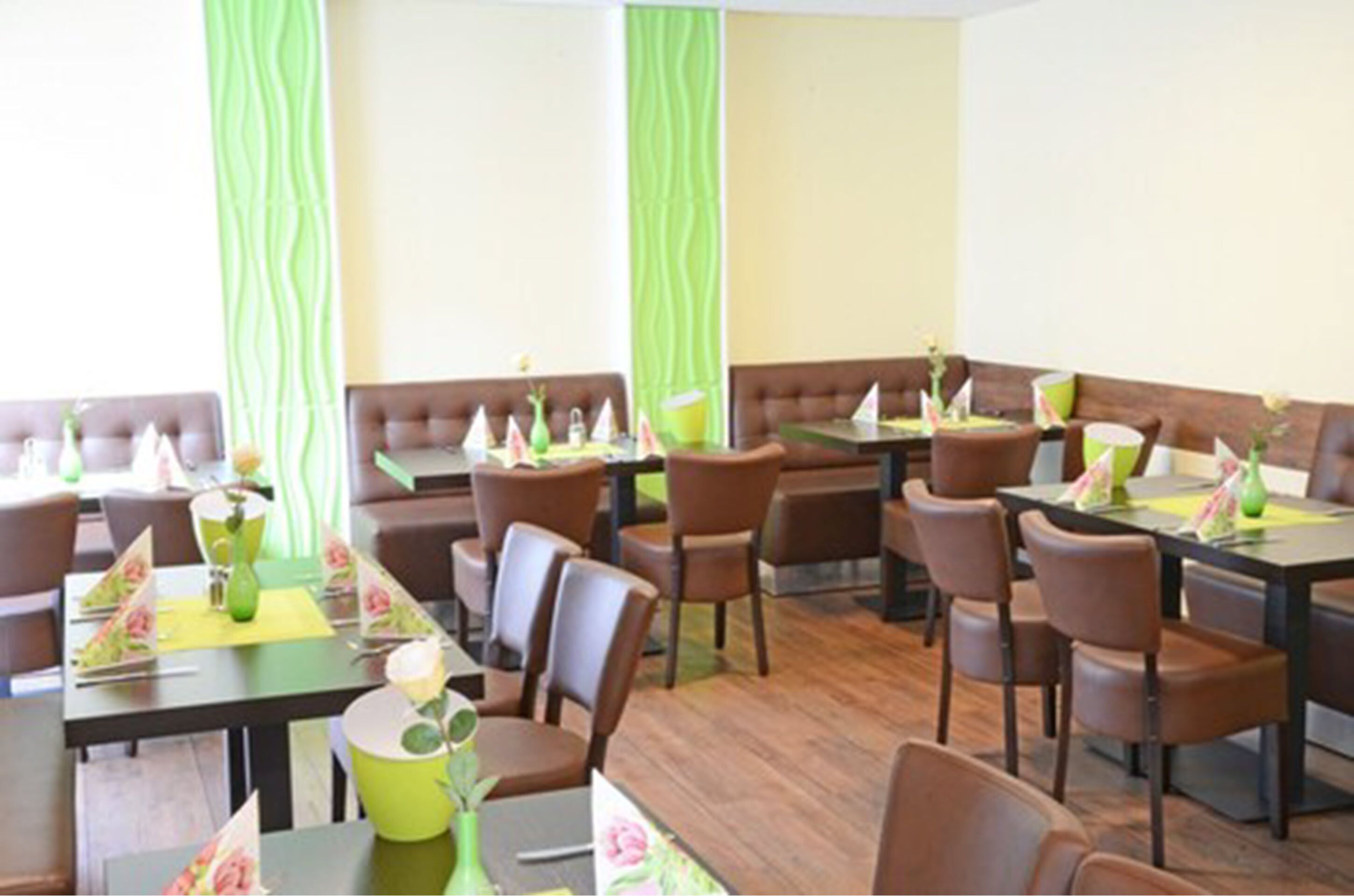Um restaurante com cabines e mesas, cortinas verdes e centros de mesa florais.