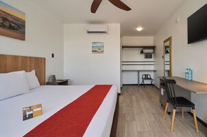 Quarto de hotel com cama, escrivaninha, cadeira, televisão e ar condicionado.