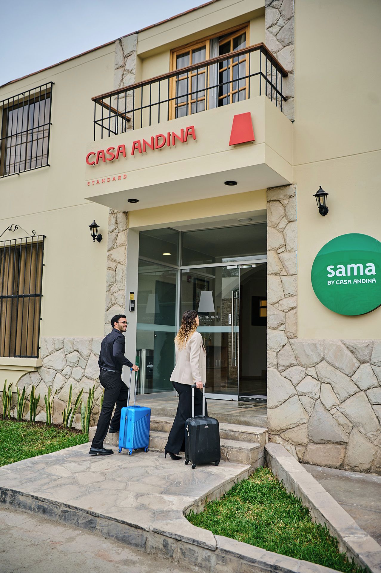 Um edifício com uma placa indicando 'CASA ANDINA STANDARD' e uma placa verde para 'sama by CASA ANDINA'.
