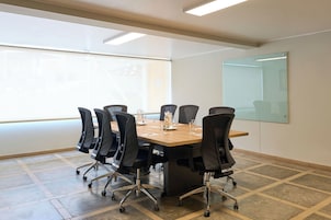 Uma sala de conferências com uma mesa comprida, cadeiras pretas e um painel de vidro.