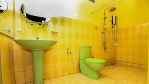 Casa de banho com azulejos amarelos, lavatório verde, sanita e chuveiro.