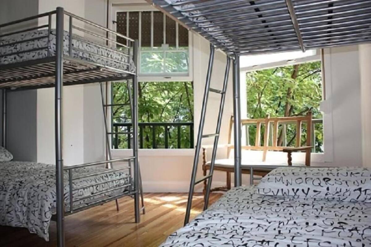 Quarto de dormitório com beliches, uma cadeira de madeira e uma janela com vista para árvores.