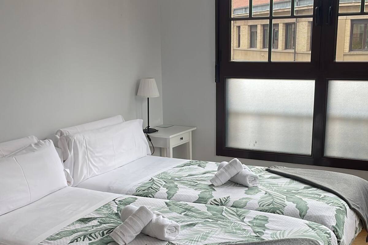 Cama bem arrumada com colcha de padrão de folhagem tropical e manta cinza.