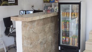 Uma área de recepção com balcão de mármore, um computador, um frigorífico cheio de bebidas e obras de arte nas paredes.