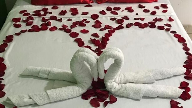 Cama com pétalas de rosas dispostas em formato de coração e duas toalhas dobradas em cisnes.