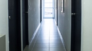 Um corredor longo e estreito com portas em ambos os lados, que conduz a um ambiente claro no final.