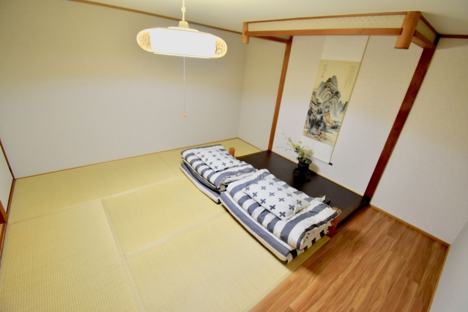 Um quarto com tatames, uma cama, um lustre pendurado e um quadro na parede.