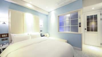 Quarto de hotel com uma cama grande, mesas de cabeceira, um rádio, um telefone, uma janela com vidro jateado e uma porta com painel de vidro jateado.