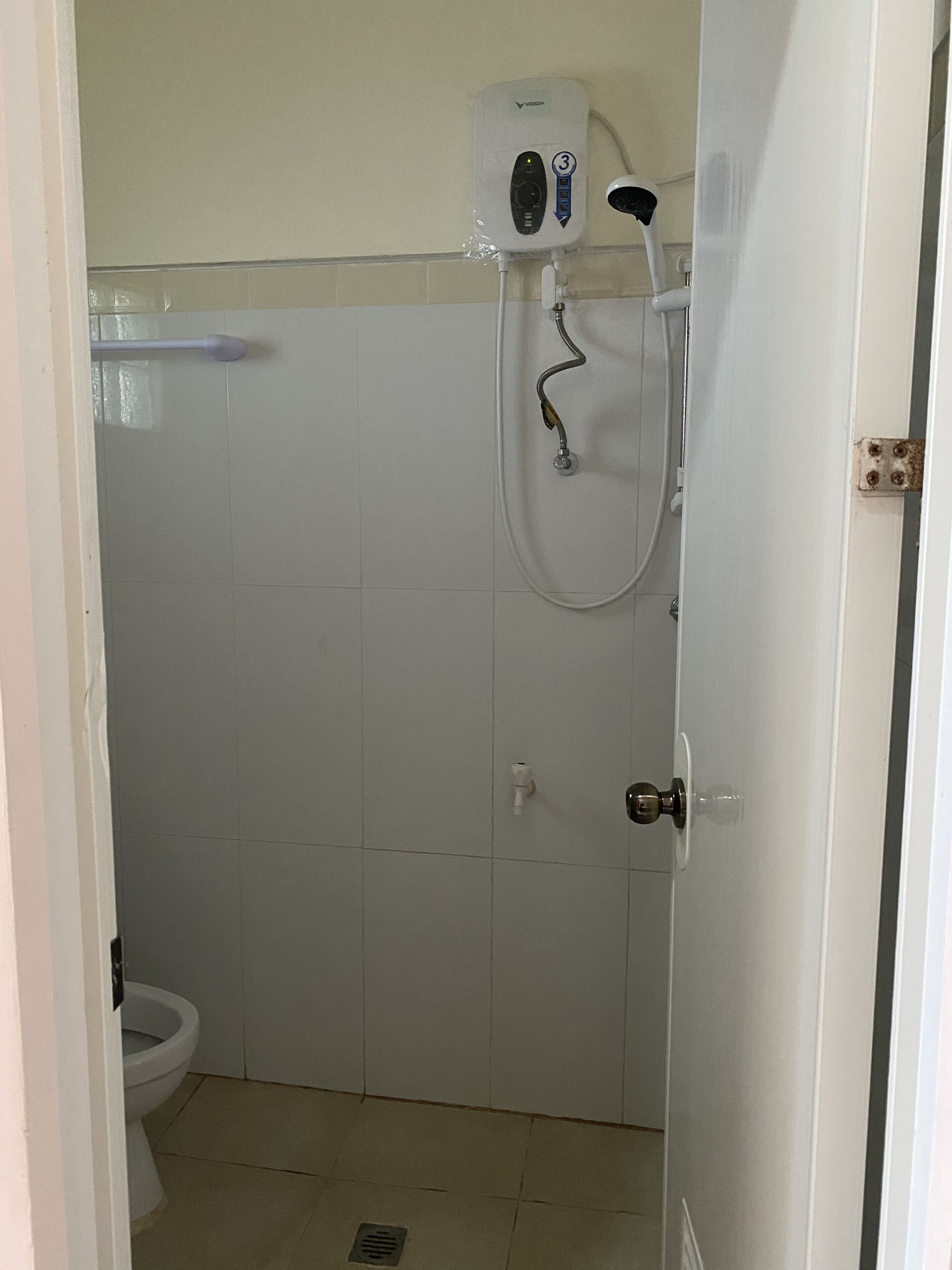 Um banheiro pequeno e fechado, com vaso sanitário, chuveiro e uma torneira fixada na parede.