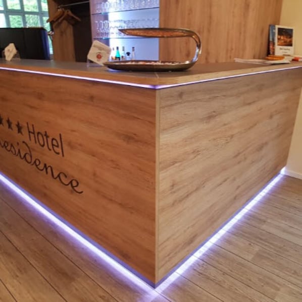 Bancada de recepção de hotel com acabamento em madeira e faixa de luz neon.