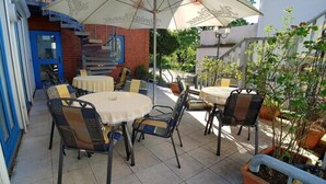 Um pátio externo com mesas e cadeiras redondas, uma escadaria e plantas em vasos.