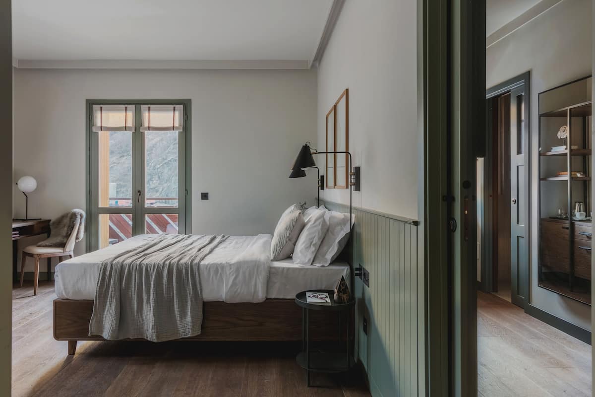 Quarto com uma cama, uma cadeira, uma escrivaninha e uma janela com cortinas.