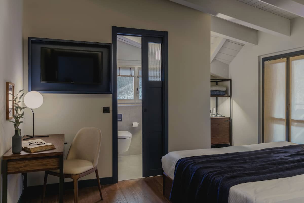 Quarto com cama, escrivaninha com cadeira, televisão e porta para um banheiro.