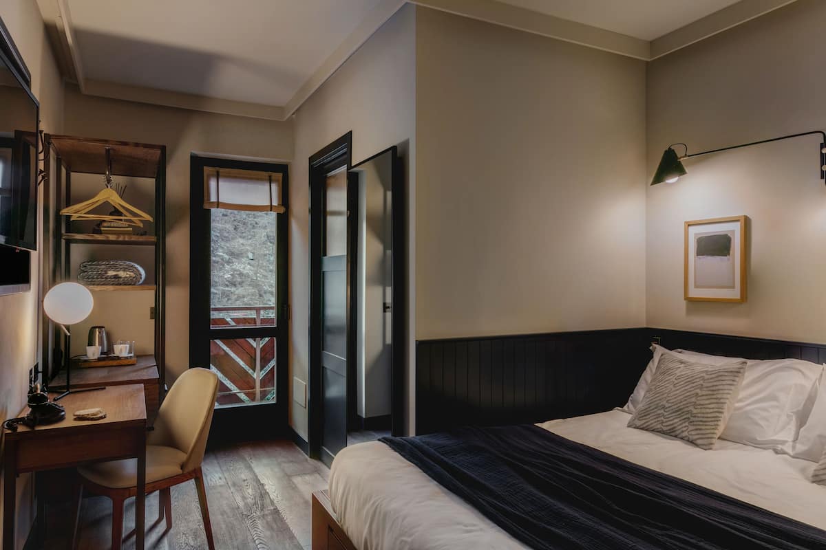 Quarto de hotel com cama, escrivaninha, cadeira e janela com vista.